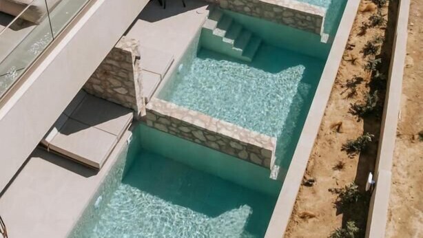 Uma piscina em vários níveis com água cristalina, degraus de pedra e área de estar externa.
