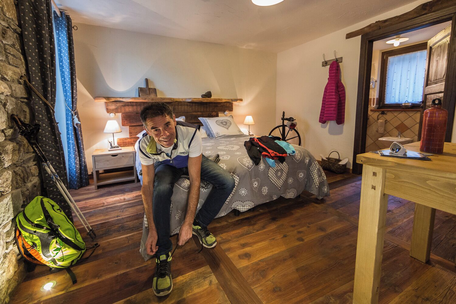 Um quarto aconchegante com uma cama, uma mesa de madeira, uma luminária e uma janela com cortinas.