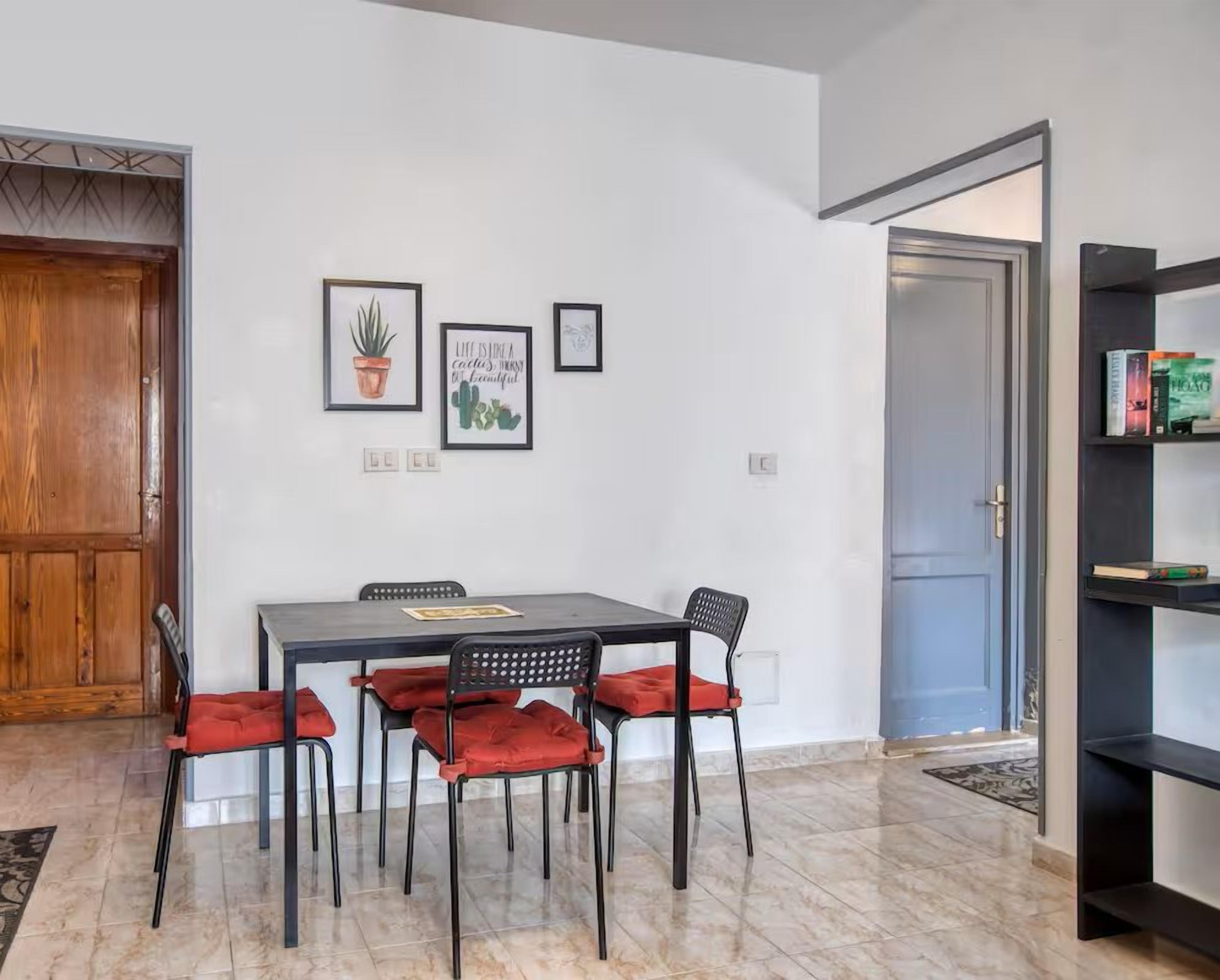 Uma sala de jantar com porta de madeira, mesa com cadeiras e obras de arte emolduradas na parede.