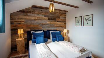 Quarto com cabeceira de madeira, duas mesas de cabeceira com abajures, cama com roupa de cama floral e duas ilustrações botânicas emolduradas na parede.