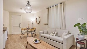 Uma sala de estar com sofá, mesa de jantar, luminária pendente, planta em vaso e uma porta.