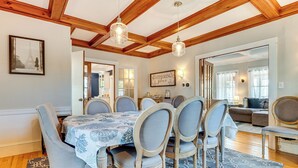 Uma área de jantar com uma mesa posta para oito pessoas, cercada por seis cadeiras, uma toalha de mesa estampada e um tapete azul.