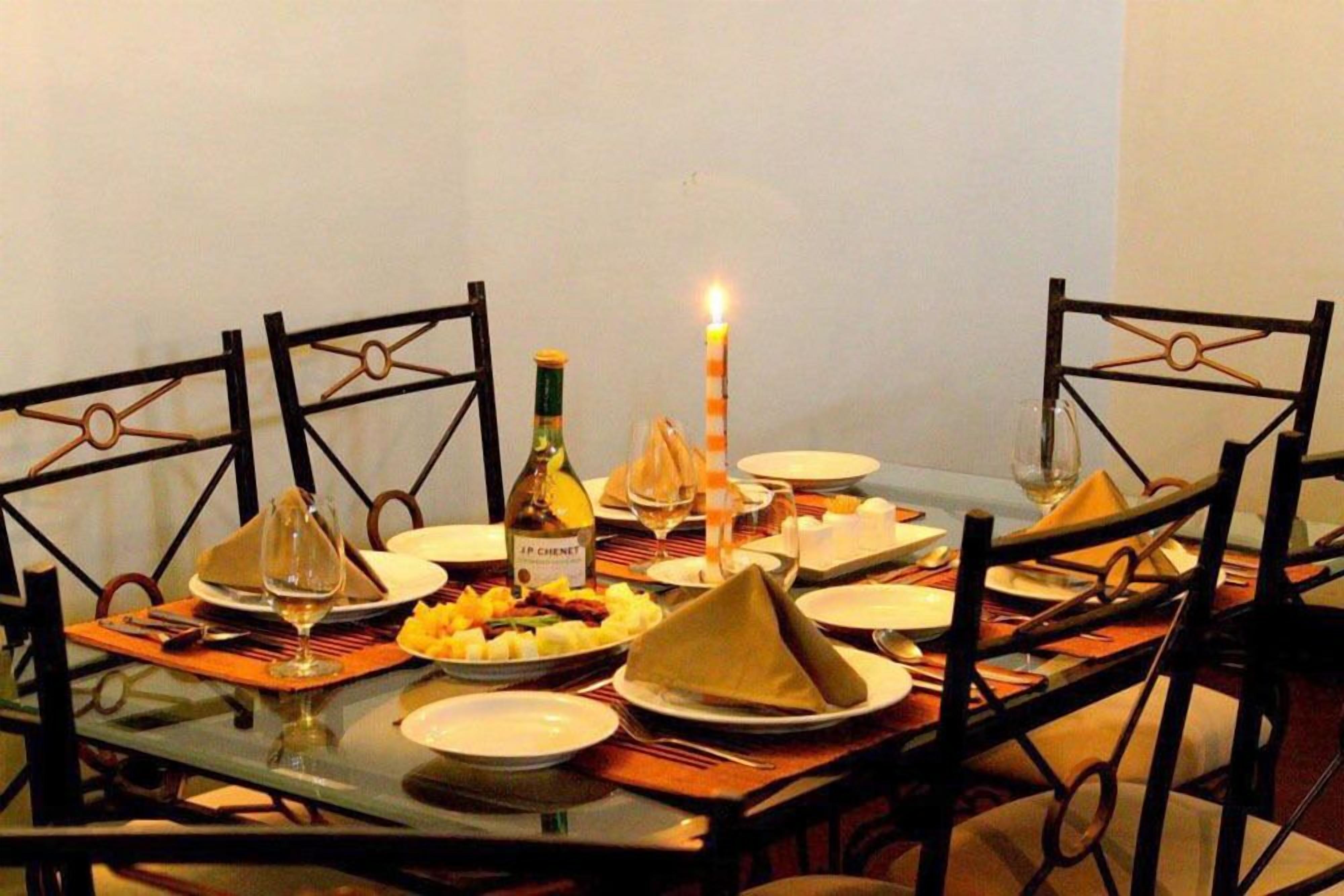 Uma mesa de jantar posta com pratos, copos, uma garrafa de vinho e uma vela acesa.