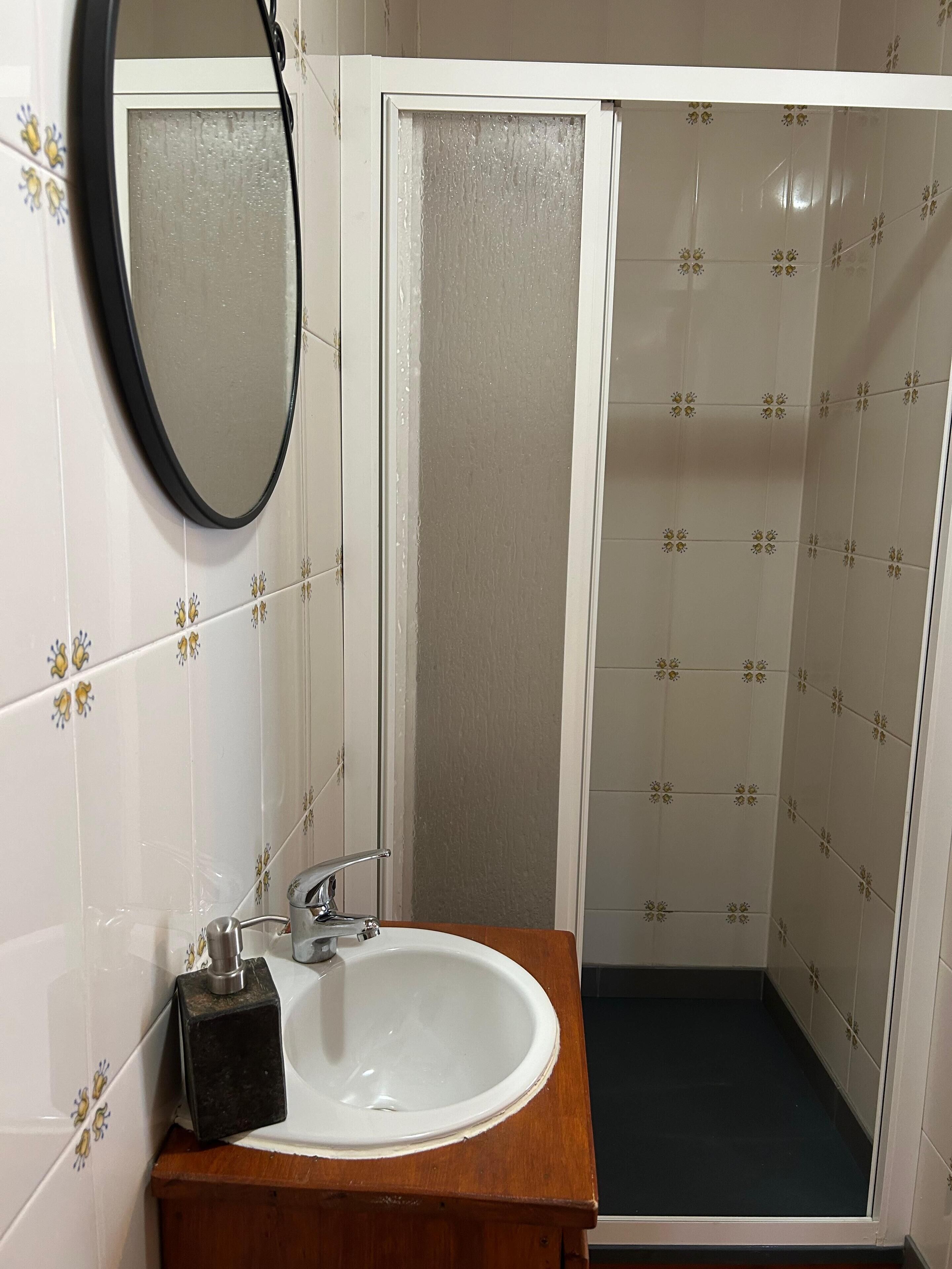 Casa de banho com lavatório branco, espelho e zona de duche.