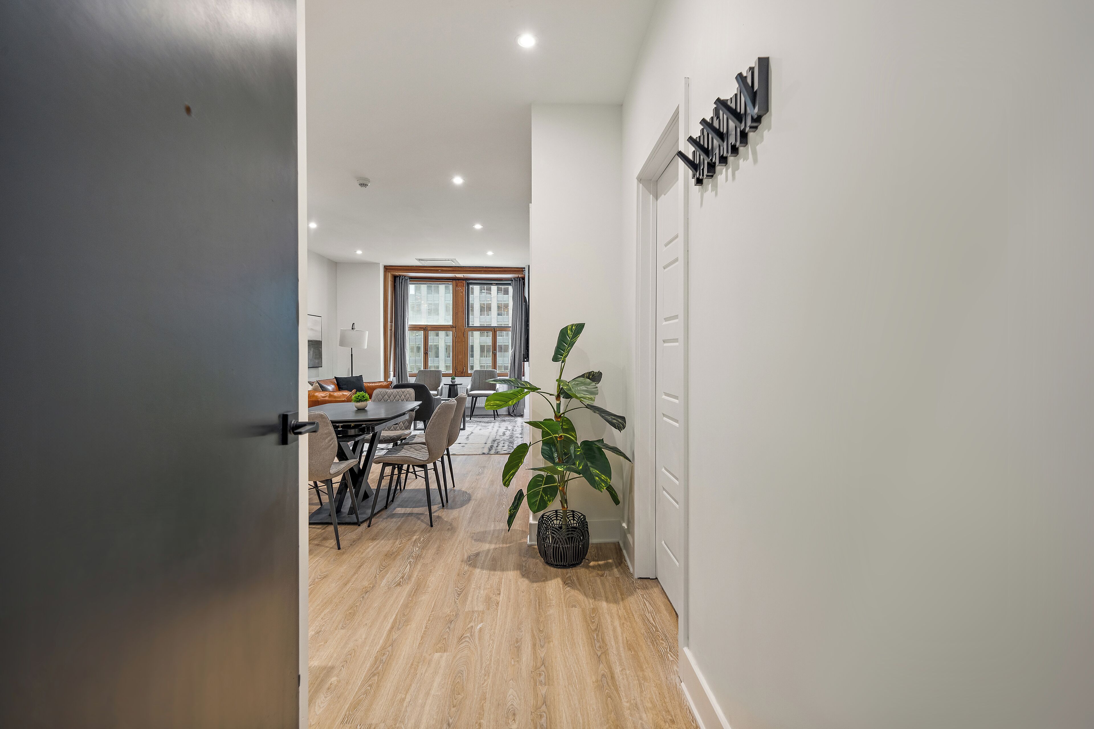 Cozinha moderna com piso de madeira, área de jantar com cadeiras e uma mesa, e uma janela grande com cortinas.
