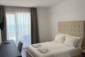Quarto de hotel com cama, escrivaninha e janela com cortinas.
