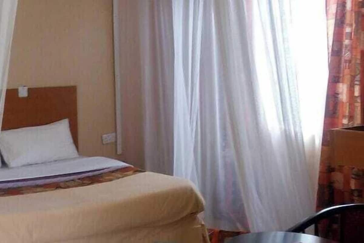 Uma cama de solteiro com cabeceira de madeira, cortinas brancas e mosquiteiro.