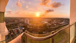 Varanda com guarda-corpo de vidro curvo, vista para a paisagem urbana ao pôr do sol.