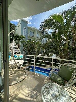 Varanda com piscina, móveis de vime branco e vista para um edifício com varandas.