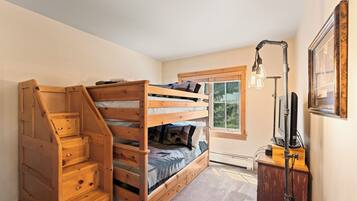 Quarto com cama de solteiro, escada de madeira, escrivaninha com luminária e janela com venezianas.