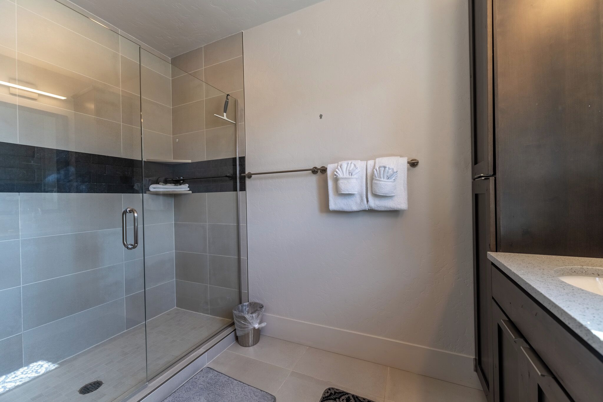 Uma casa de banho moderna com cabine de duche em vidro, um porta-toalhas com duas toalhas e um frigorífico de aço inoxidável.