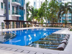 Uma piscina com água azul cristalina, rodeada por edifícios modernos e palmeiras.