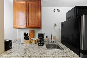 Uma cozinha com armários de madeira, geladeira preta, cafeteira e pia.
