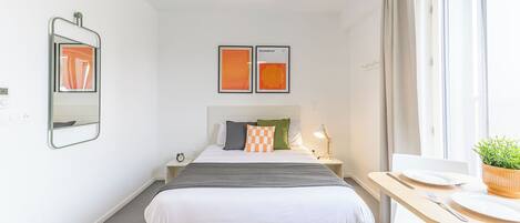 Quarto de hotel moderno com cama, mesa de cabeceira, luminária e janela com cortinas.
