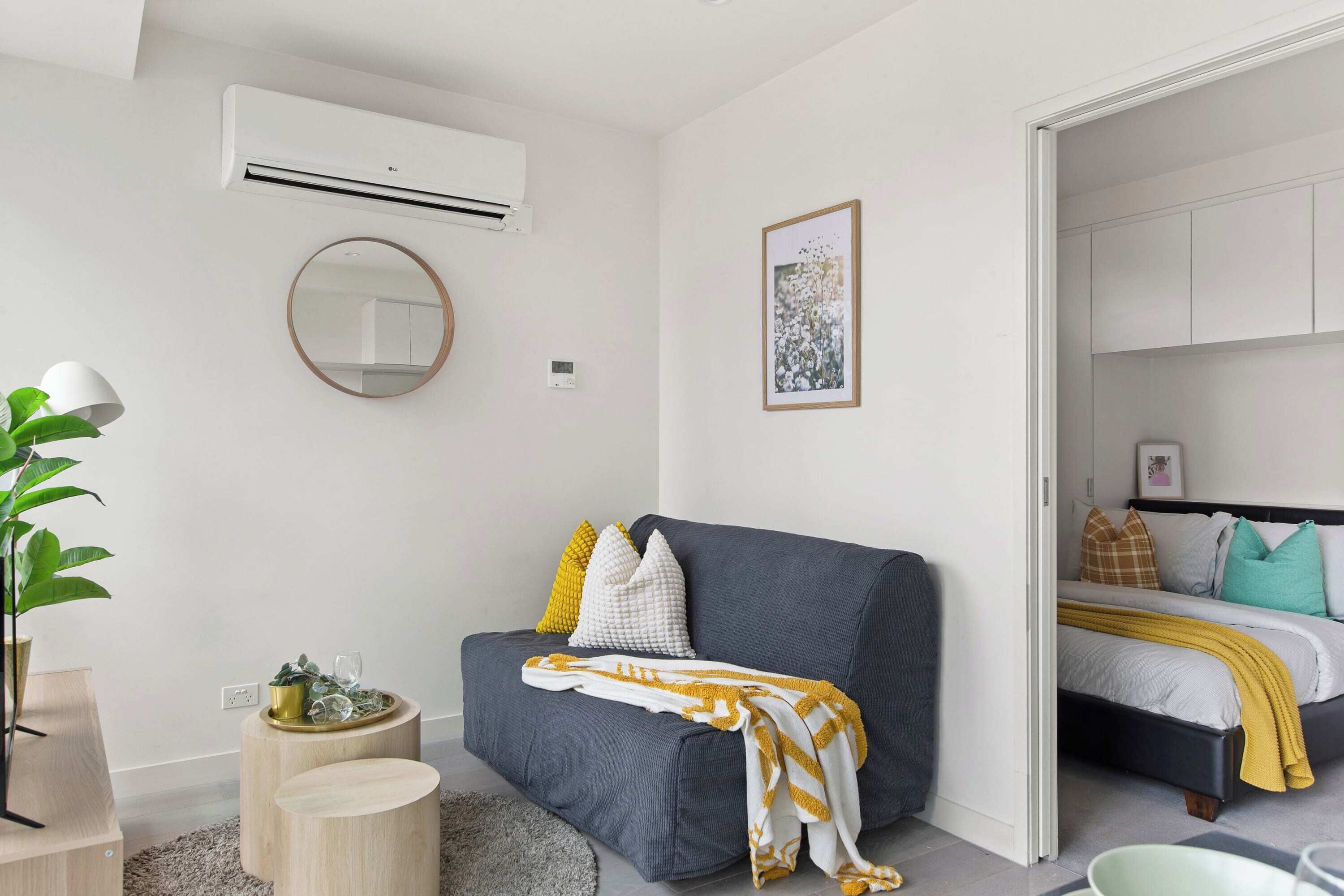 Uma sala de estar moderna com um sofá cinzento, um espelho redondo e uma pequena mesa lateral de madeira.