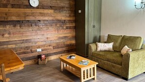 Uma sala de estar acolhedora com uma parede de madeira, um sofá verde, uma mesa de centro de madeira e um relógio na parede.