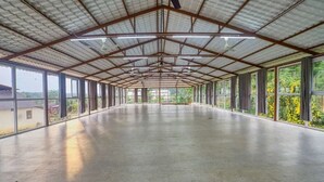 Um edifício amplo e vazio em estilo industrial, com teto alto, estrutura metálica e grandes janelas que dão para áreas verdes no exterior.