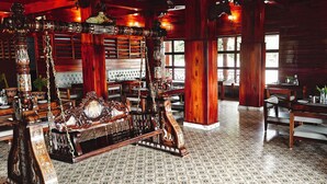 Interior tradicional em madeira com mobiliário elaborado, incluindo uma cama de madeira entalhada e uma mesa de jantar.