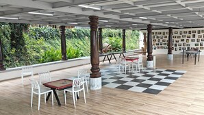 Um espaço interior com chão quadriculado, pilares de madeira, cadeiras brancas e uma parede com quadros.