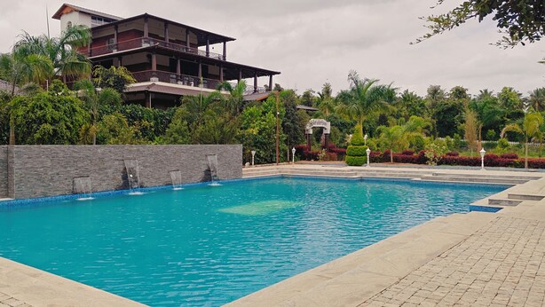 Piscina com muro de pedra, cercada por vegetação exuberante e um edifício com varandas.