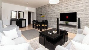 Uma sala de estar moderna com um sofá cinza, uma mesa de centro preta e uma TV instalada em uma parede texturizada.