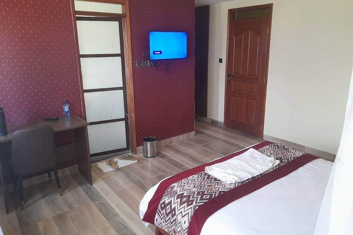 Quarto de hotel com cama, escrivaninha, televisão e porta.
