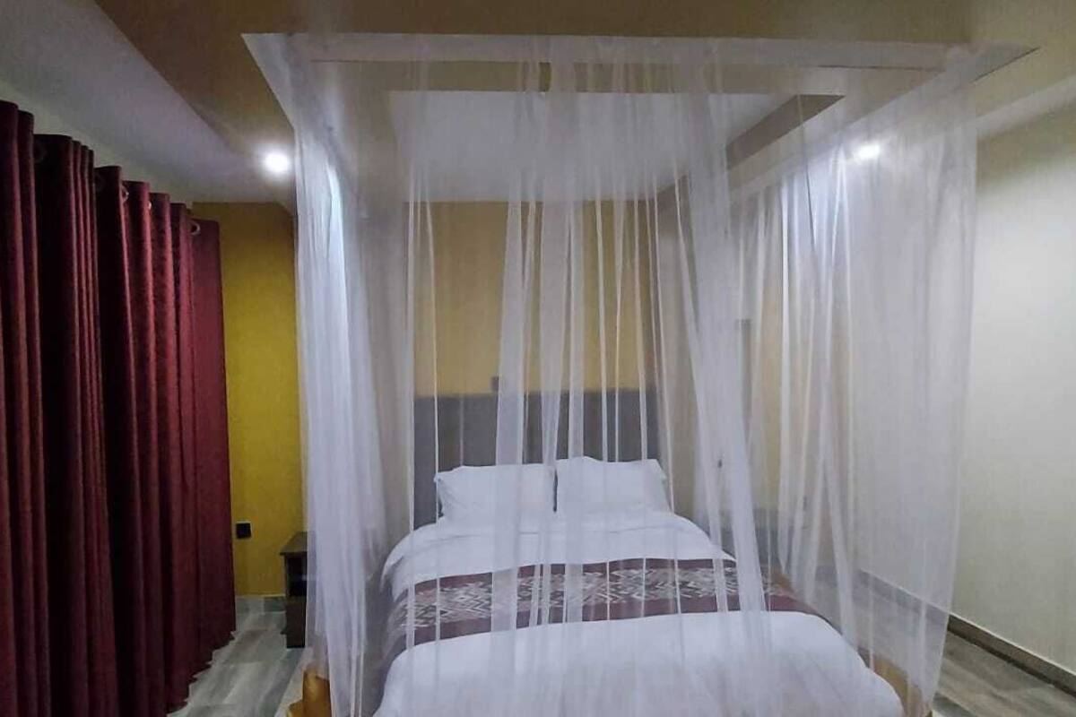 Quarto com cama sob um dossel branco, cortinas vermelhas de um lado e parede lisa do outro.