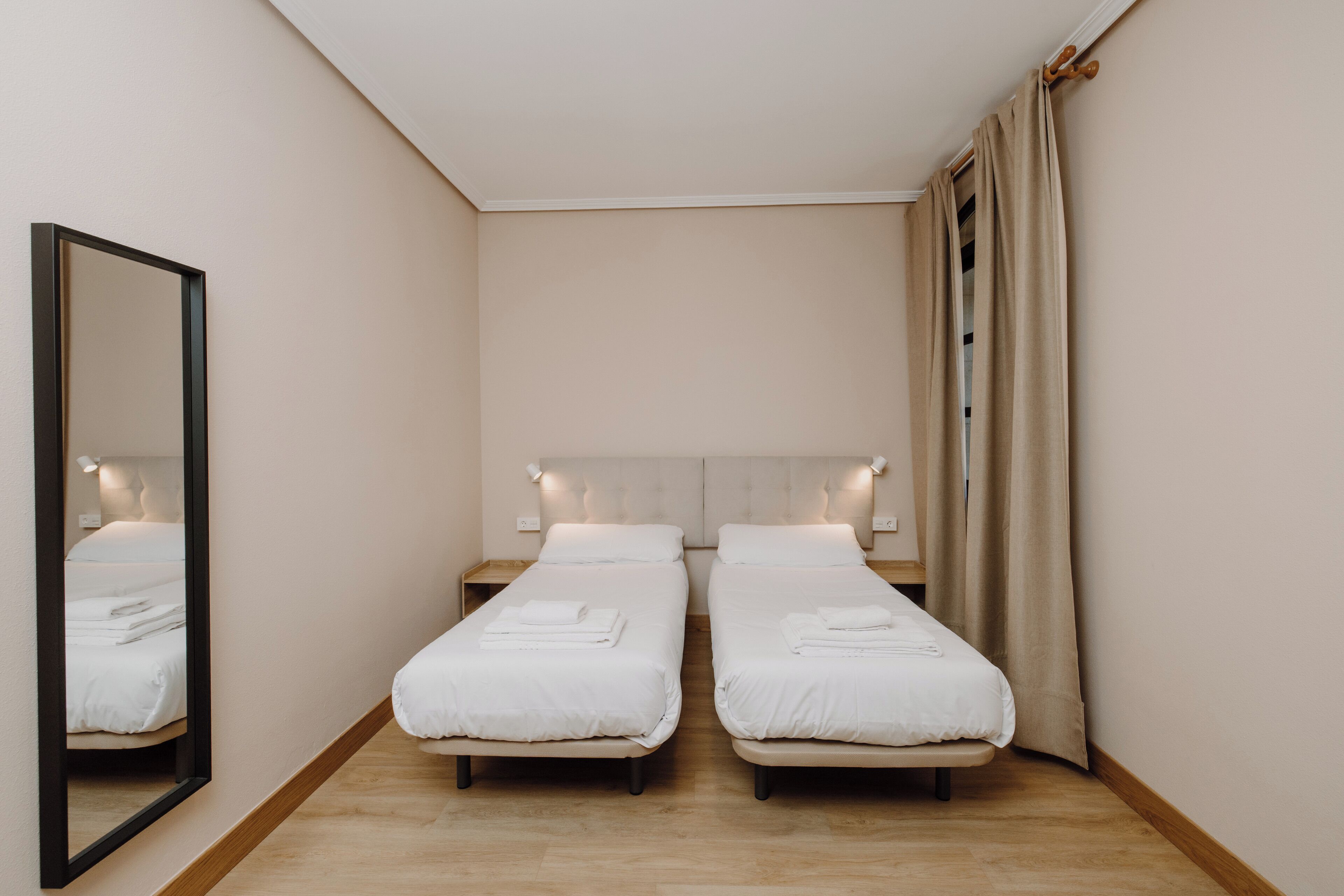 Quarto de hotel com duas camas de solteiro, um espelho grande e piso de madeira.