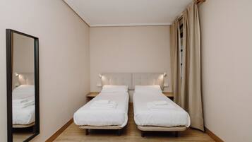 Quarto de hotel com duas camas de solteiro, um espelho grande e piso de madeira.