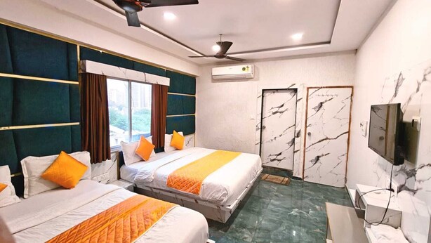 Quarto de hotel com duas camas, um ventilador de teto, ar condicionado, parede com padrão marmorizado e televisão montada na parede.