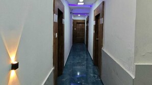 Um corredor estreito com chão em azulejos azuis, iluminação embutida no teto e um ponto de luz fixado na parede.