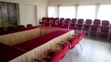 Uma sala de conferências com uma mesa comprida e cadeiras vermelhas, grandes janelas e um quadro na parede.
