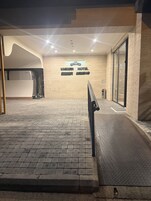 Entrada de hotel com piso de azulejos, corrimão de metal e placa com o nome do hotel.