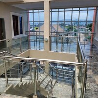 Um espaço interior em vários níveis, com guarda-corpos de vidro e vista para a paisagem urbana através de grandes janelas.