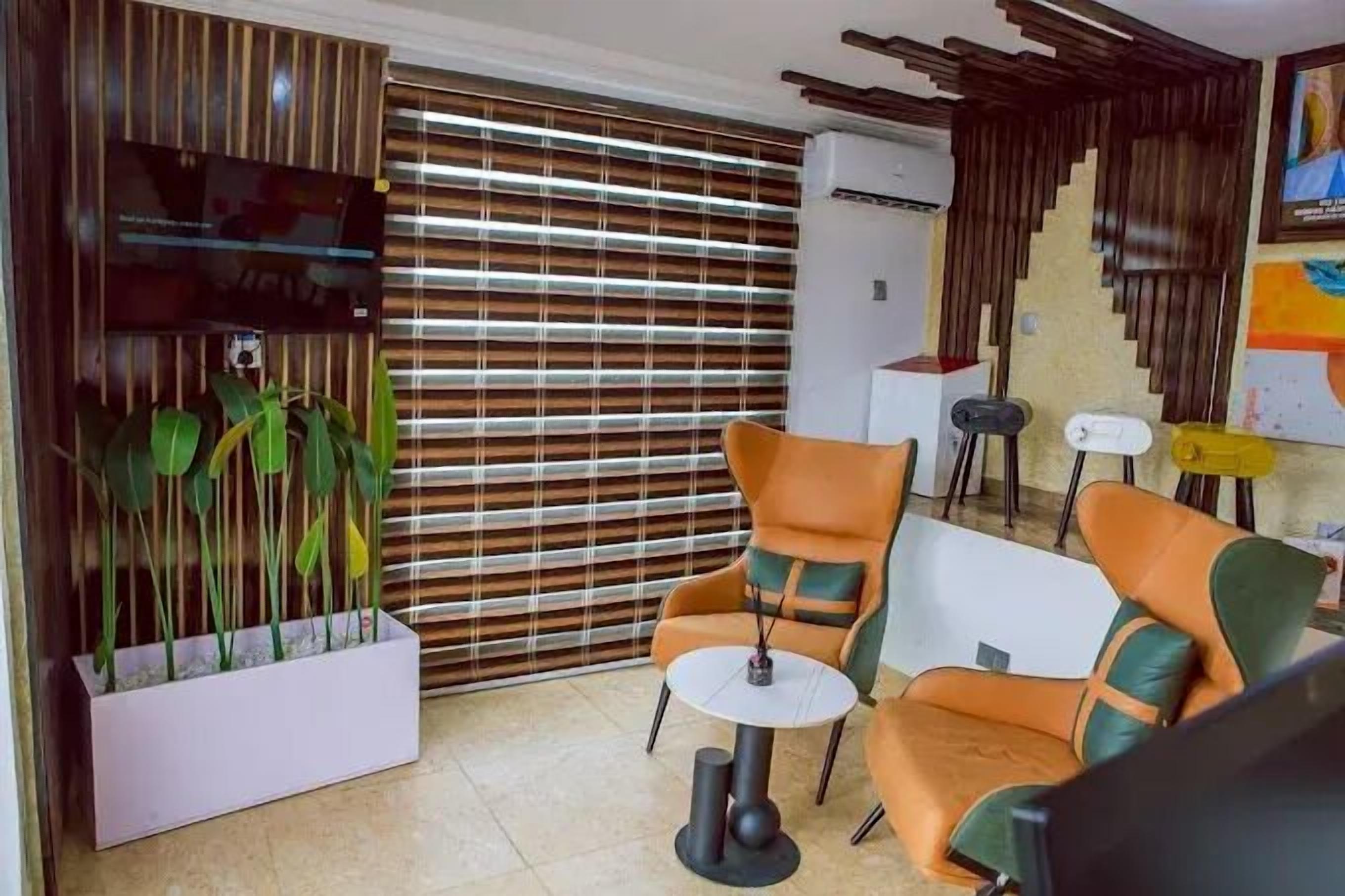 Uma sala de estar moderna com televisão, duas poltronas laranja e verde, uma mesinha e uma planta.