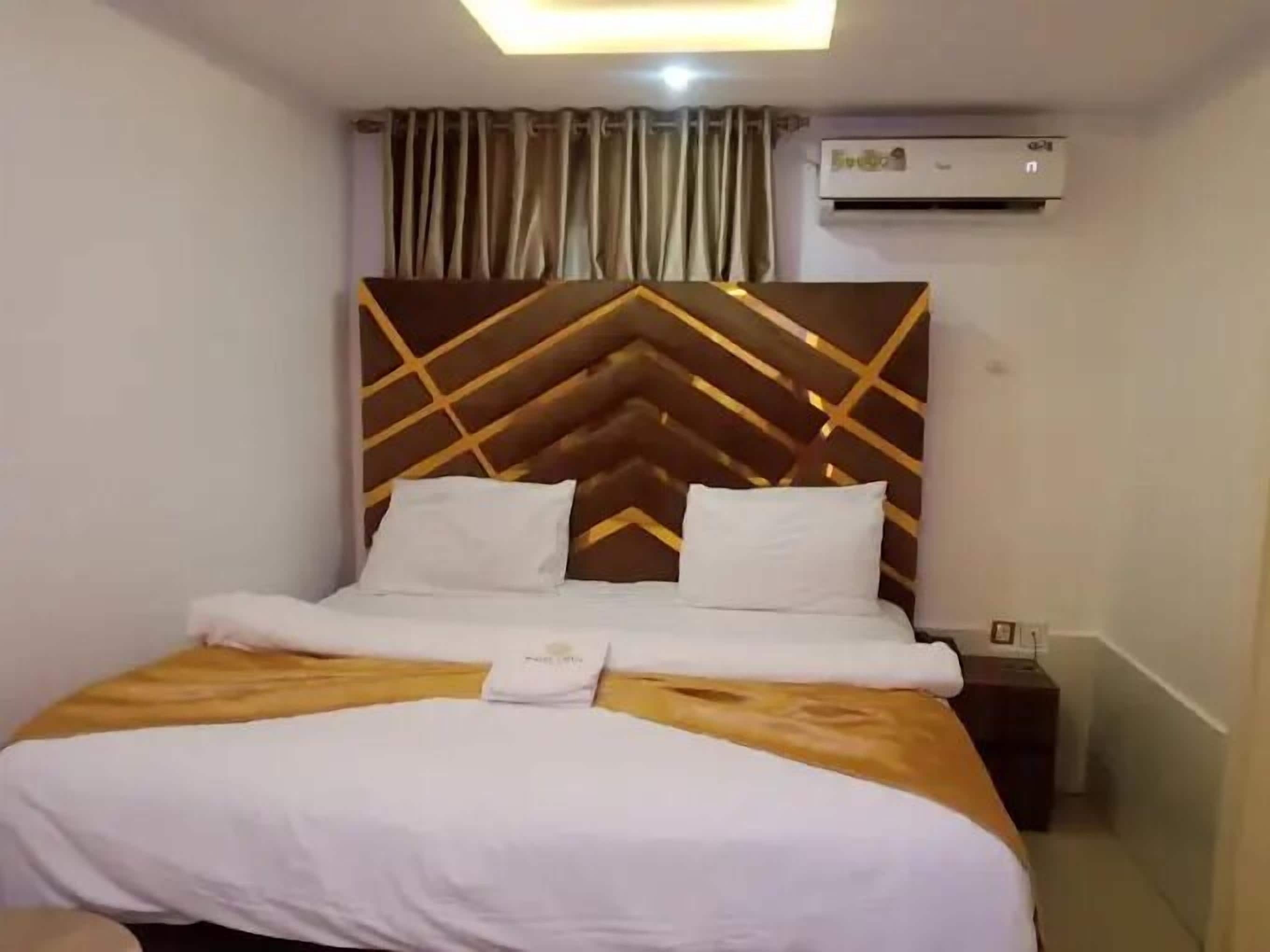 Quarto de hotel com uma cama moderna, mesa de cabeceira e ar condicionado.