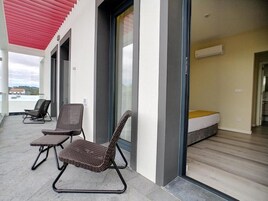 Quarto de hotel moderno com uma grande porta de vidro deslizante que dá para uma varanda com cadeiras de vime.