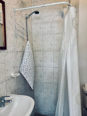 Uma casa de banho com chuveiro, pia e porta-toalhas.