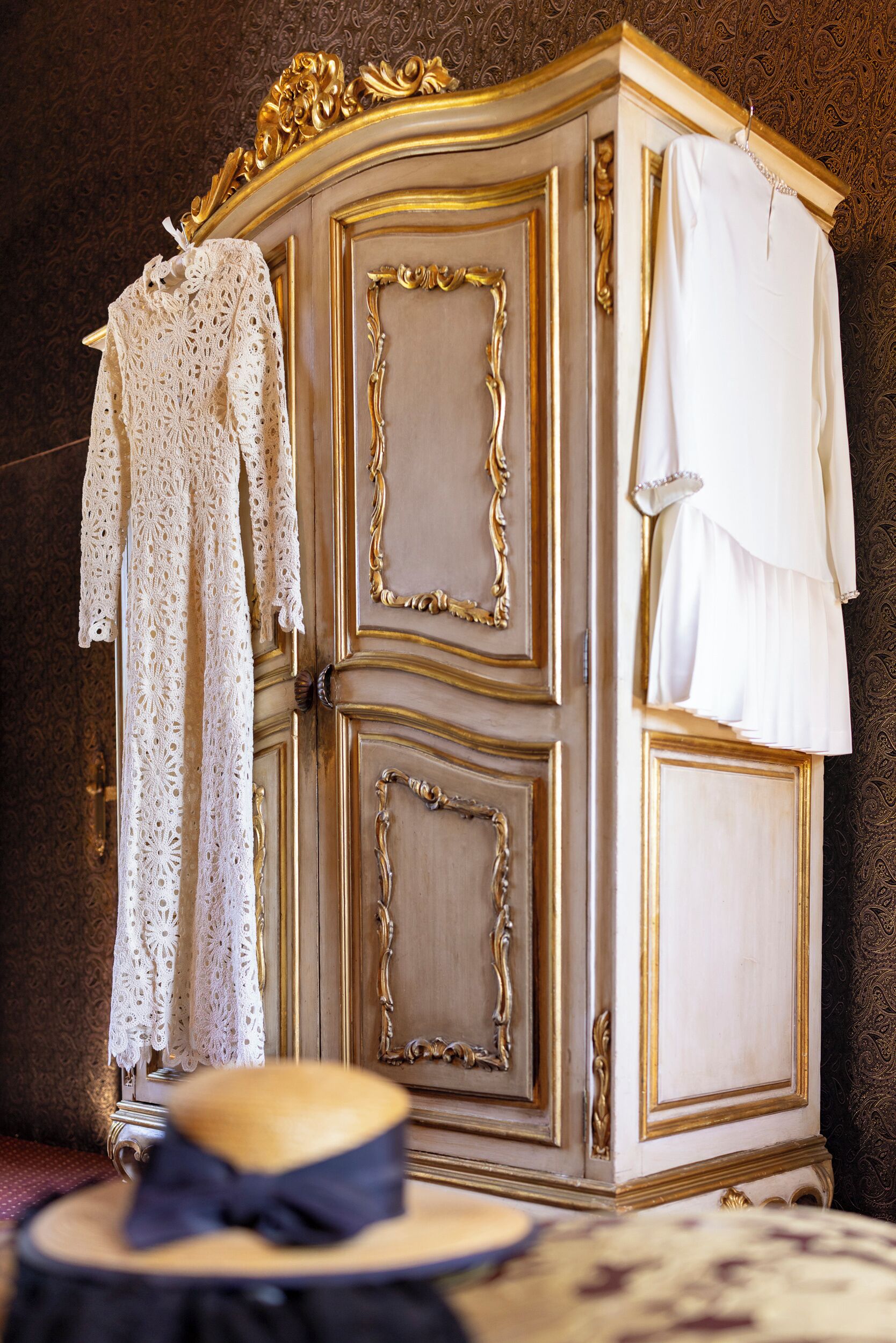 Guarda-roupa de estilo antigo com detalhes dourados elaborados e um espelho.