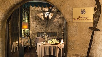 Interior com parede de pedra, mesa posta para refeição e placa indicando 'Restaurant La Tour du Chateau'.