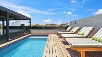 Área de piscina no terraço, com espreguiçadeiras e um espaço de estar coberto.