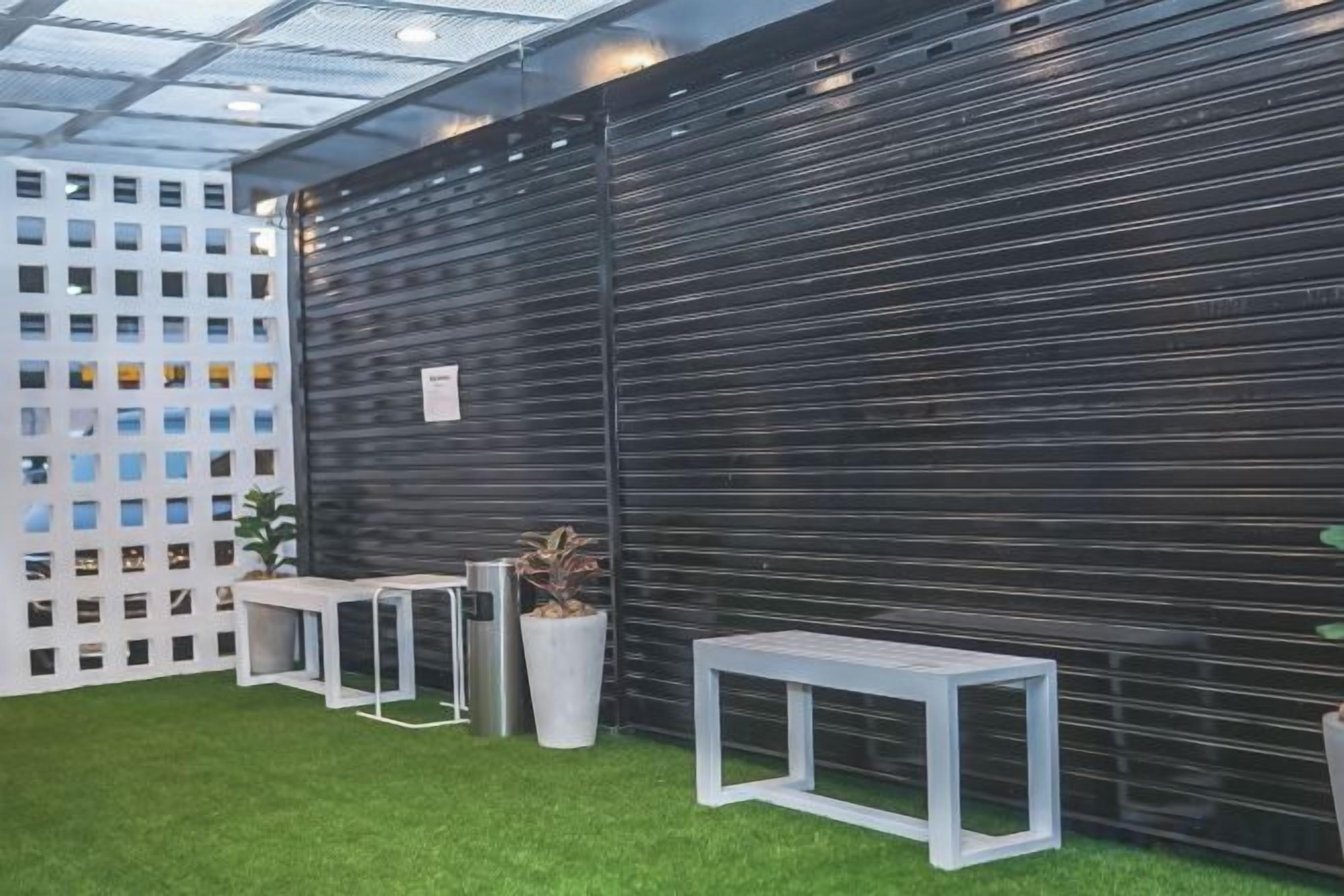 Espaço interior com grama sintética, parede de metal e mobiliário branco.