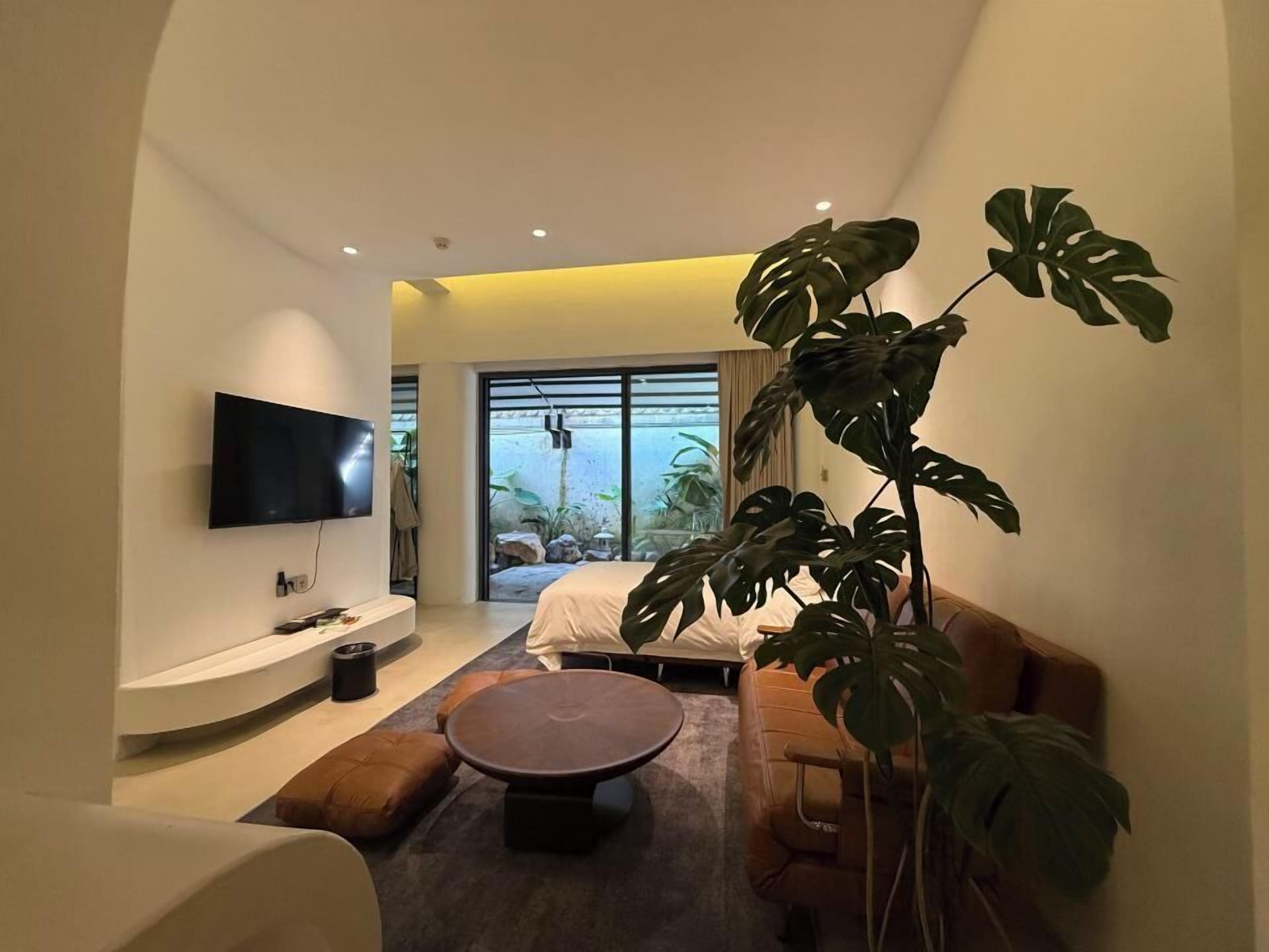 Uma sala de estar moderna com uma televisão de tela plana, um sofá, uma mesa de centro e uma planta grande.