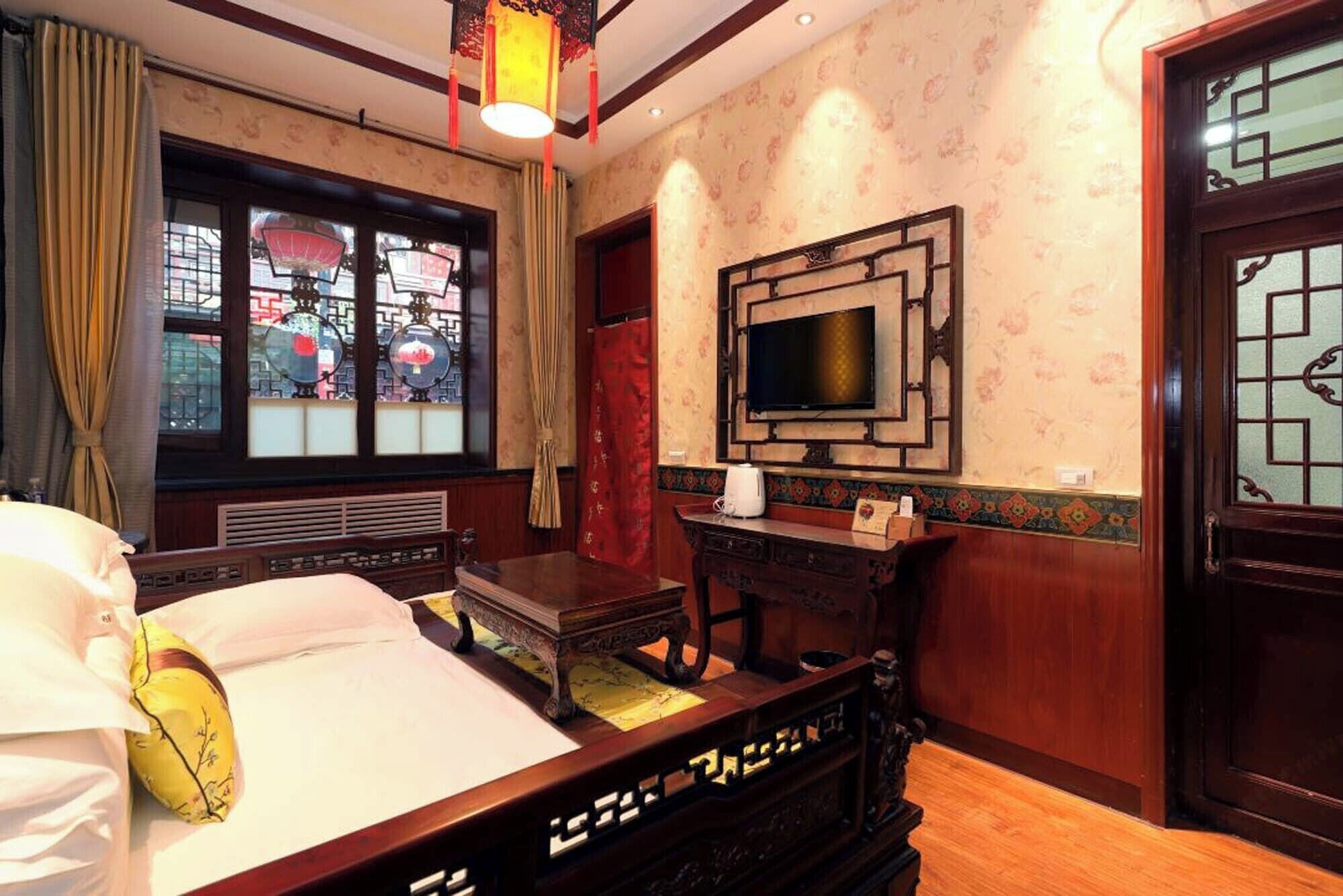Quarto tradicional com uma cama, televisão na parede e janela com detalhes decorativos.