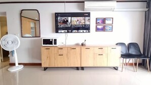 Quarto moderno com um armário de madeira, uma TV de tela plana na parede, um ventilador de chão e duas cadeiras pretas.