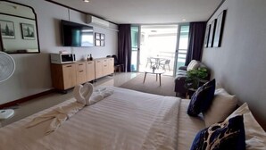 Quarto de hotel com uma cama grande, uma escrivaninha com computador, televisão de tela plana e varanda com mesa e cadeiras.