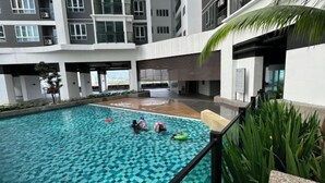 Uma piscina com piso em azulejos, cercada por um edifício com varandas e uma área coberta.