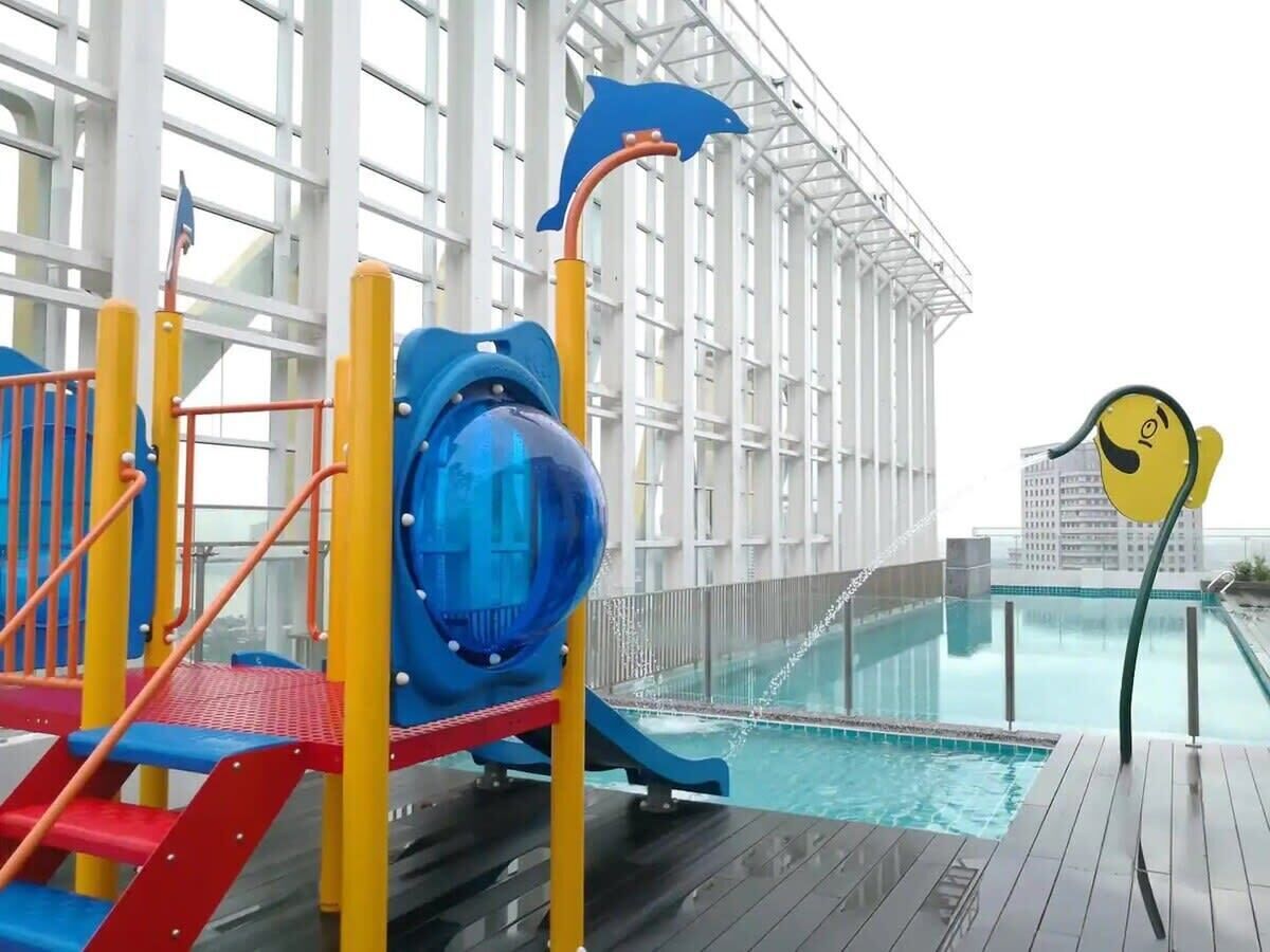 Espaço infantil com escorregadores e estruturas de escalada, piscina e vista para um edifício moderno.