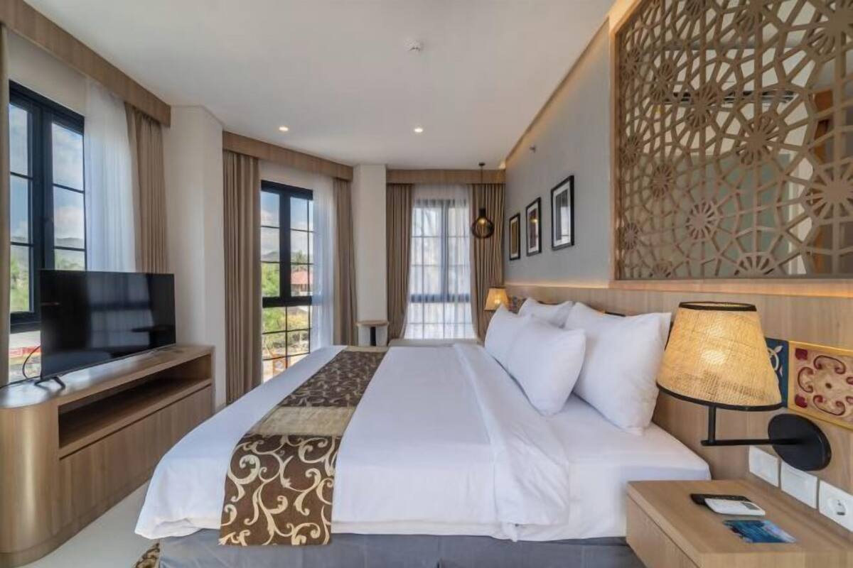 Quarto de hotel com uma cama grande, televisão, secretária e um painel decorativo na parede.