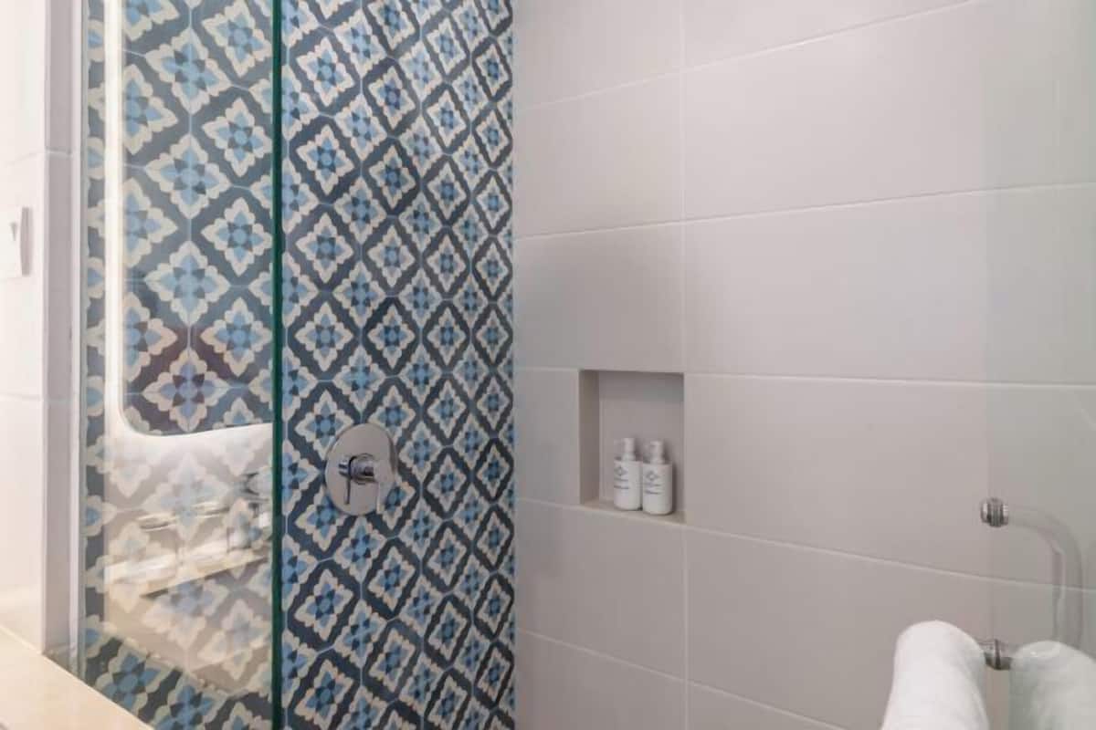 Casa de banho com azulejos estampados, cabine de duche em vidro, lavatório branco e um porta-toalhas.